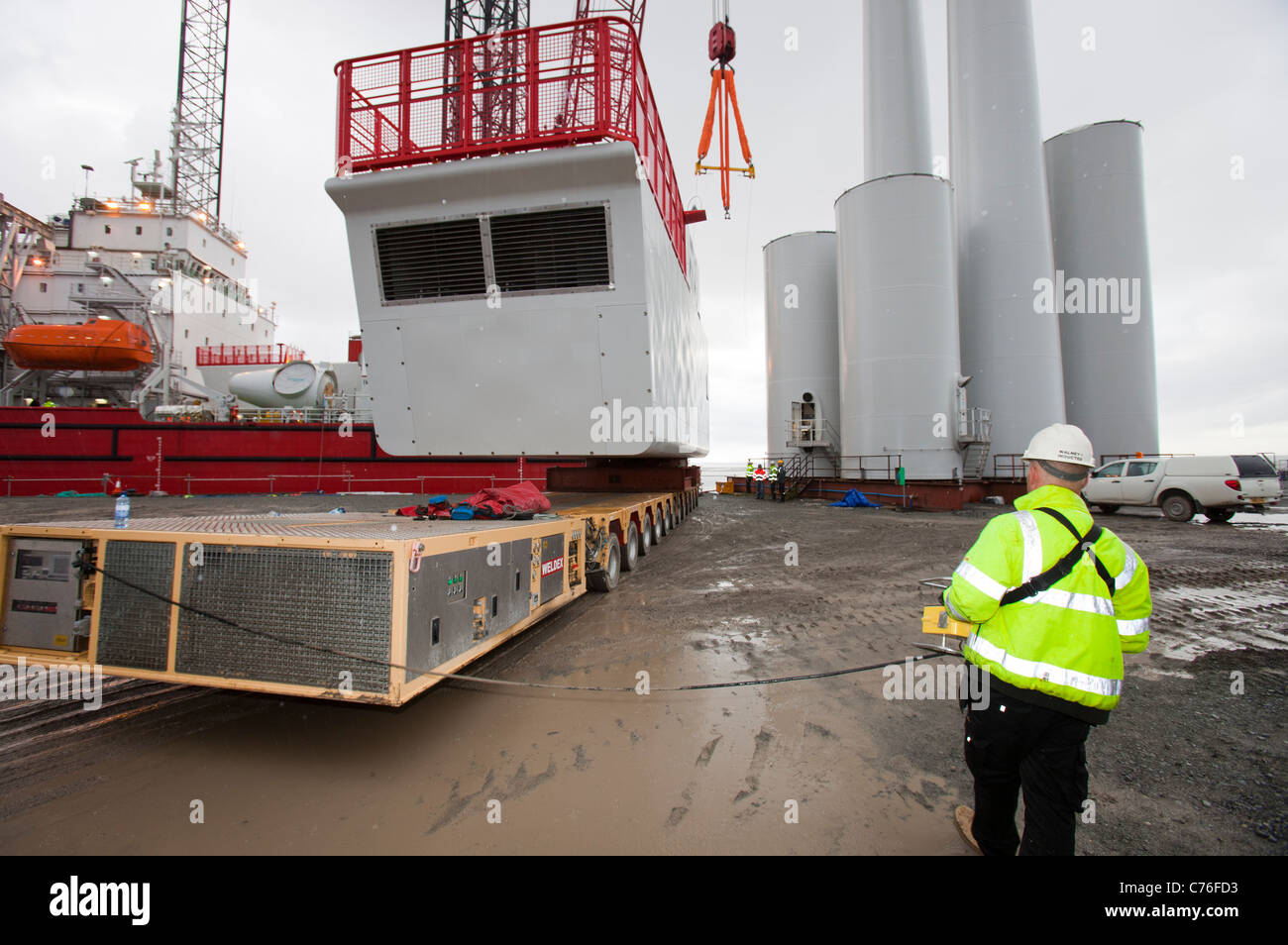 Workers lift a nacelle for a wind turbine onto a jack up barge, for the ...