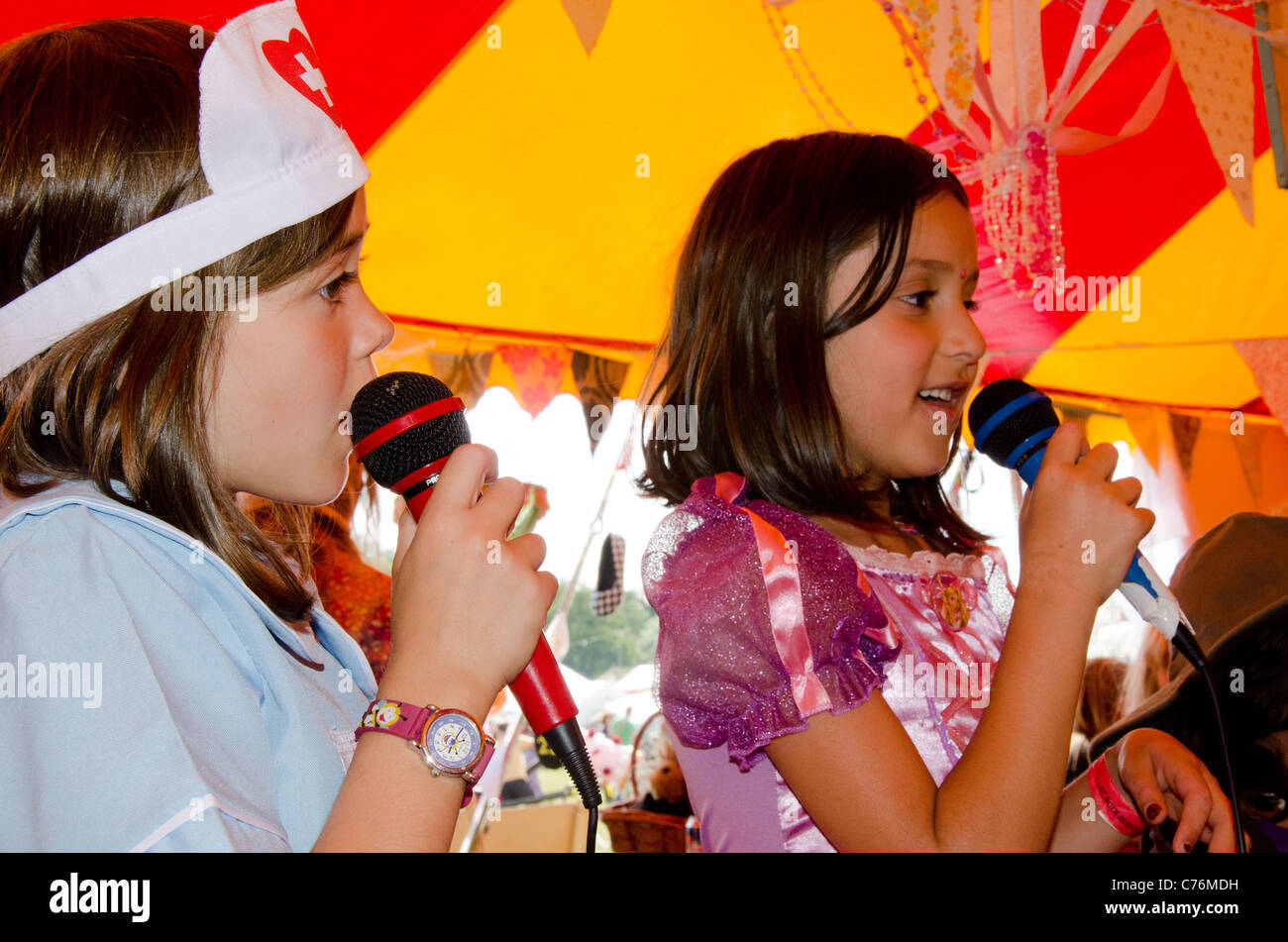 Two girls singing karaoke in a tent in fancy dress at Shambala Festival ...