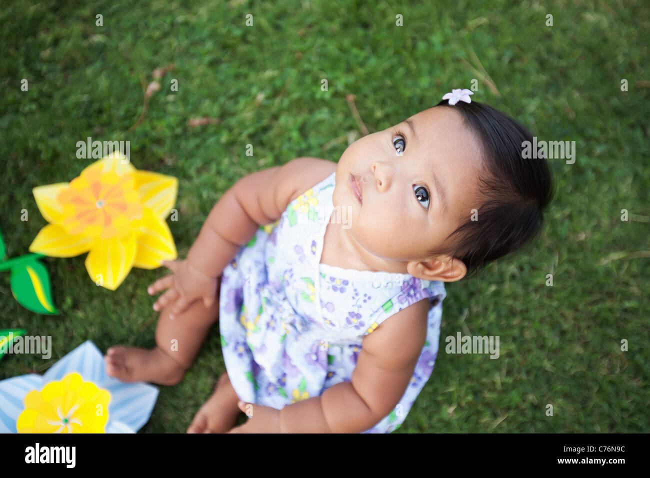Cute baby girl looking up at the sky sitting on the lawn with pinwheels ...