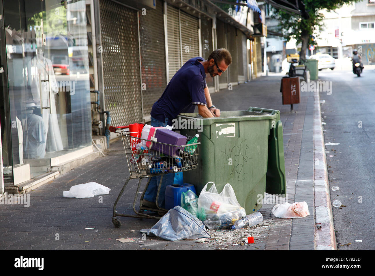 A homeless person looking for useful waste in garbage bin in southern ...