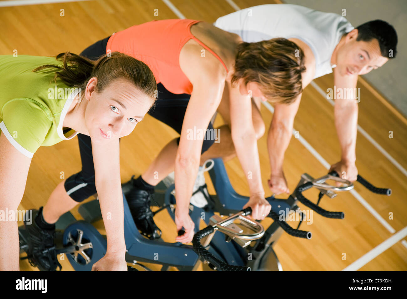 Three people cycling in a gym or fitness club, dressed in colorful ...