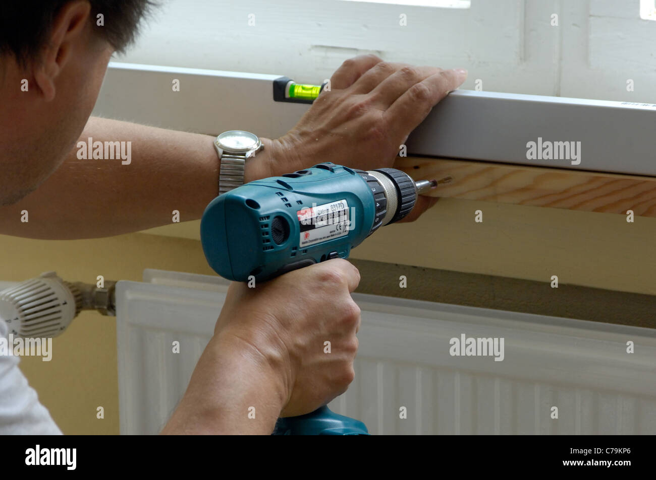 Workman screwing a wooden board to a wall Stock Photo - Alamy