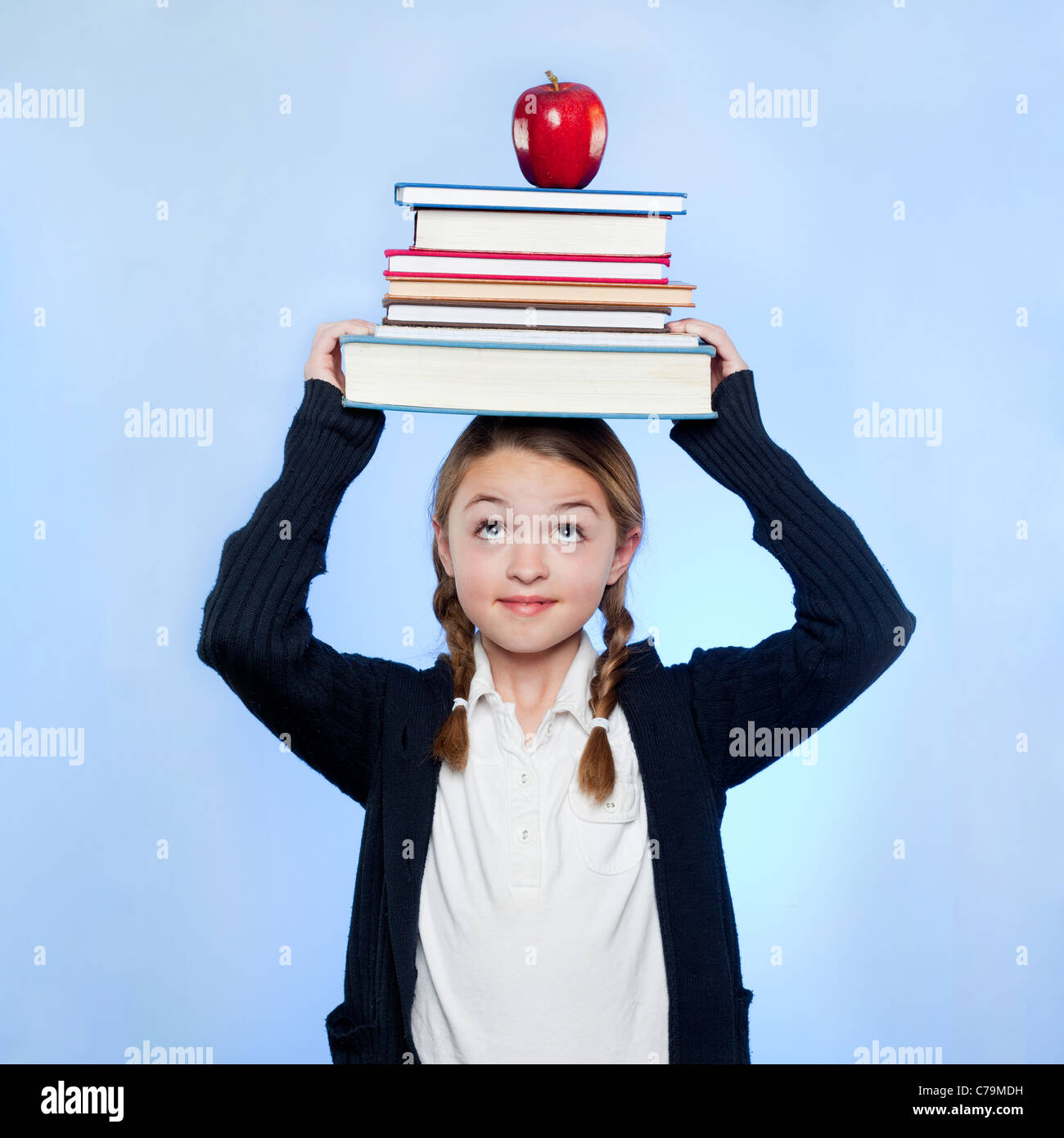 Studio shot of girl (10-11) holding stack of books and apple on head ...