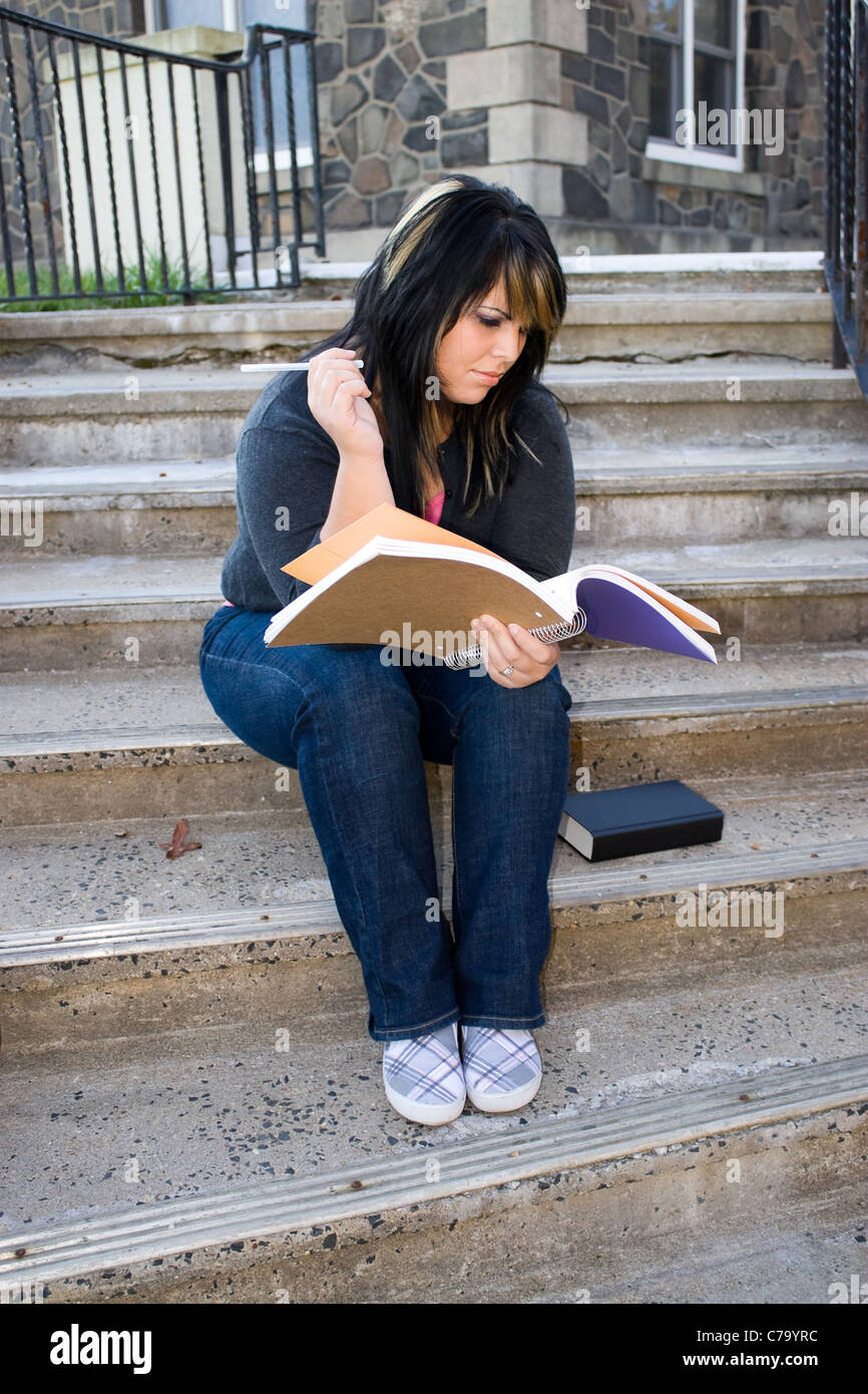 A young woman looking at her notebook while sitting on the campus ...