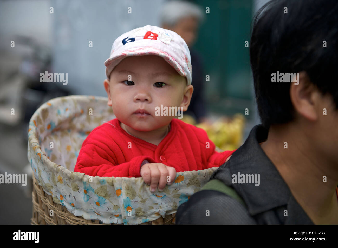Chinese migrant woman carrying a baby on her back with a bamboo basket ...
