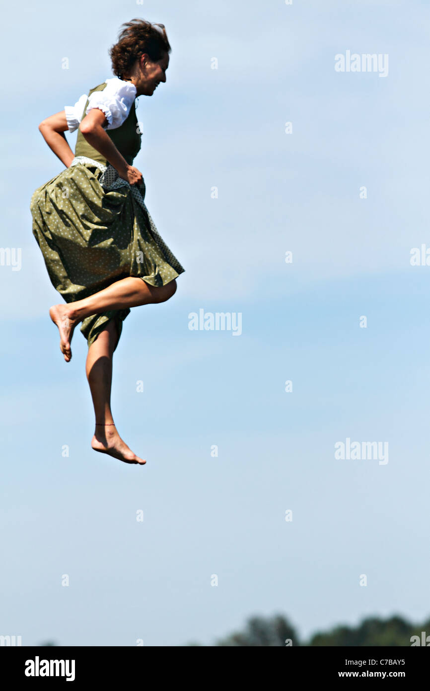 Woman in traditional bavarian dress jumping through the air into Lake ...