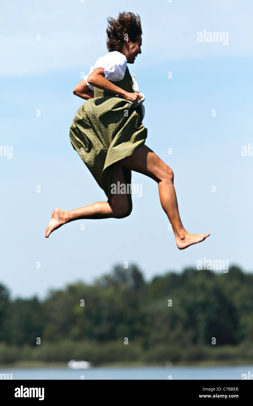 Woman in traditional bavarian dress jumping through the air into Lake ...