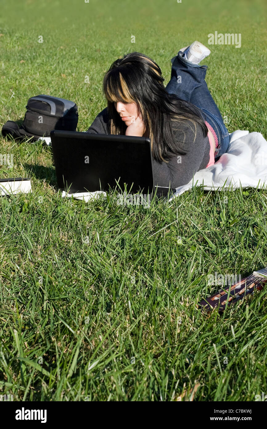 A young student using her laptop computer while laying in the grass on ...