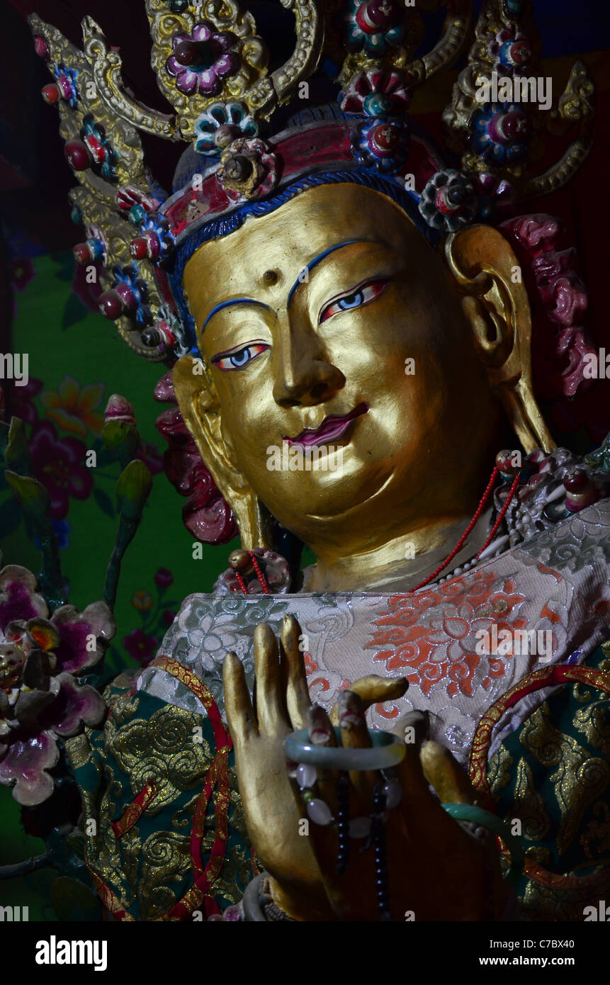 A golden statue with colourful headgear gazes compassionately downwards ...