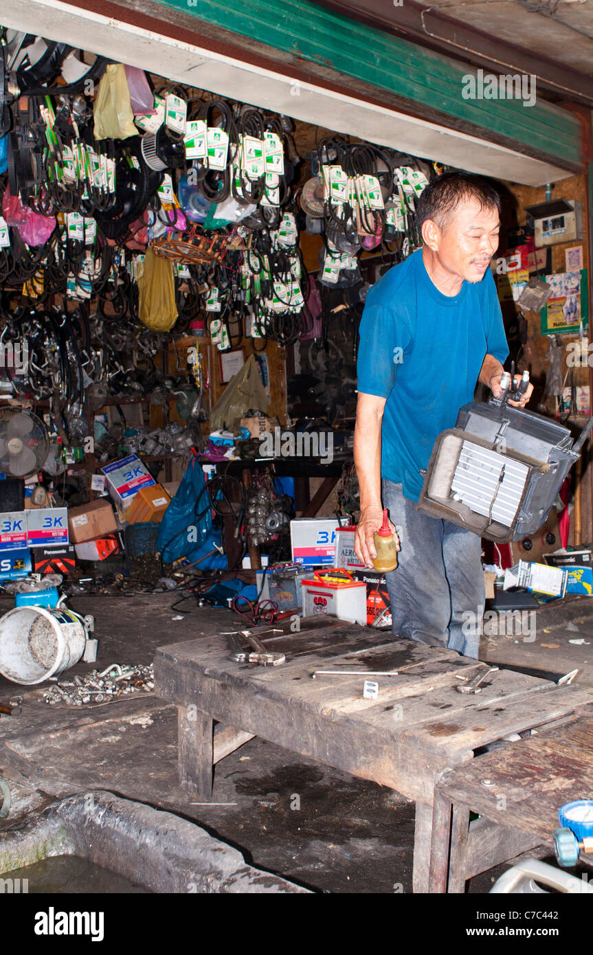 Thai Mechanic carrying a radiator in a messy garage in Bangkok Thailand ...