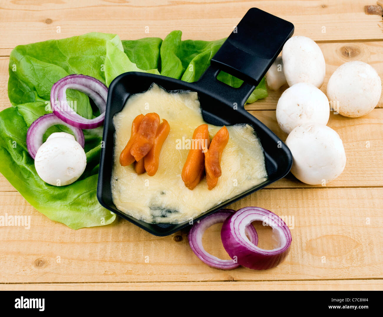 Raclette pan with cheese and cocktail sausages on wooden background ...