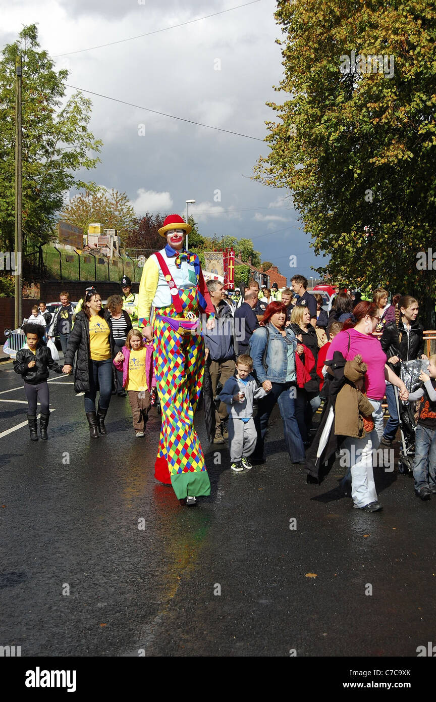 Clown in full costume on stilts walking with parade crowd in Gorton ...
