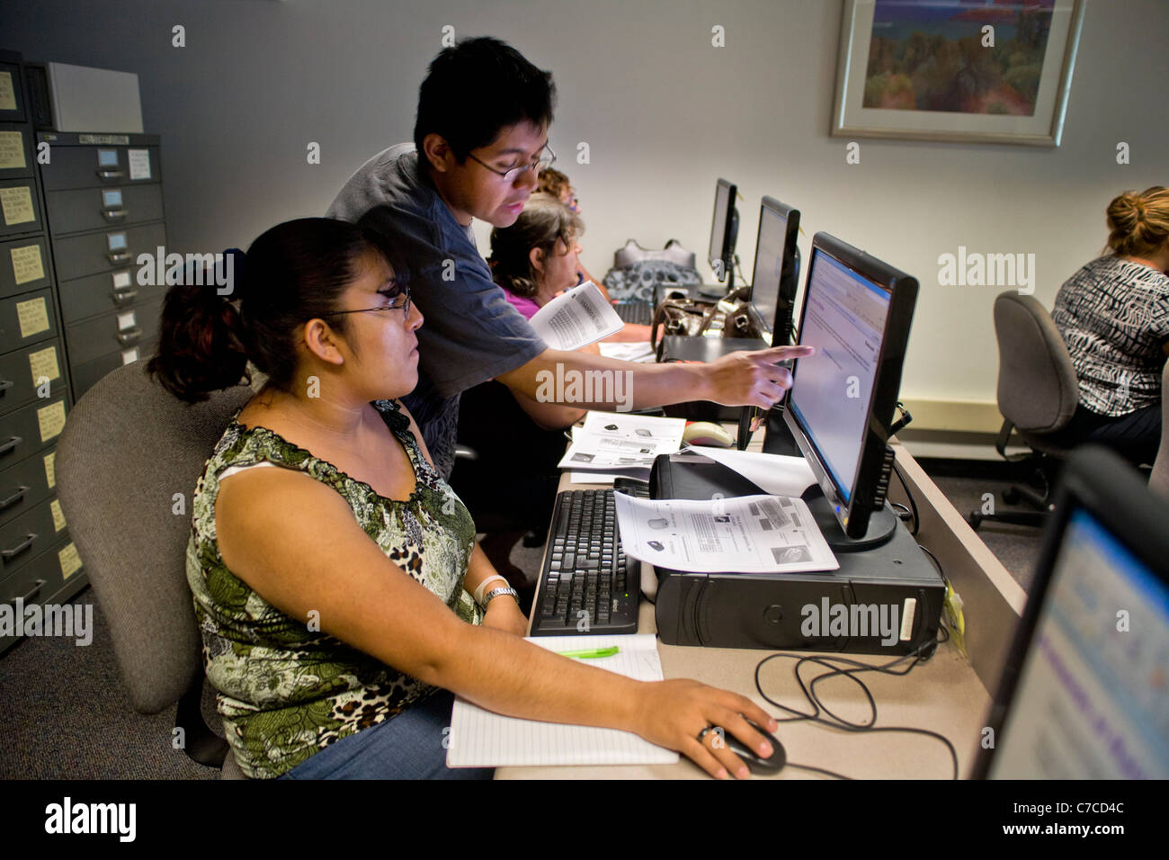A young Hispanic teacher helps Hispanic students of different ages in a ...