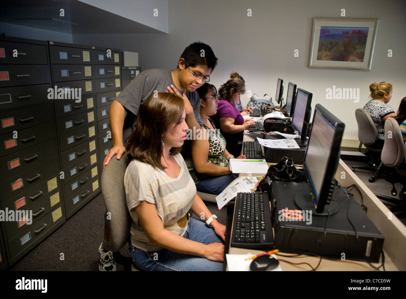 A young Hispanic teacher helps Hispanic students of different ages in a ...