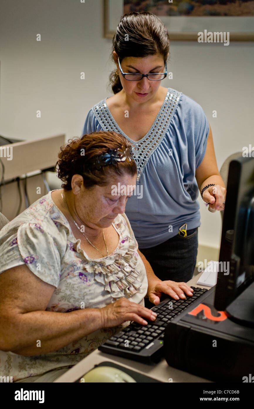 A young Hispanic teacher helps a senior Hispanic woman in a basic ...