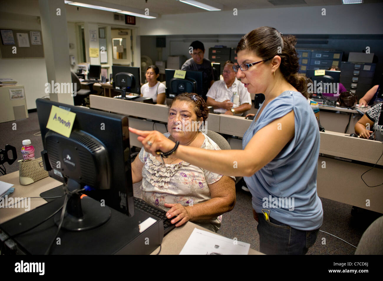 A young Hispanic teacher helps a senior Hispanic woman in a basic ...