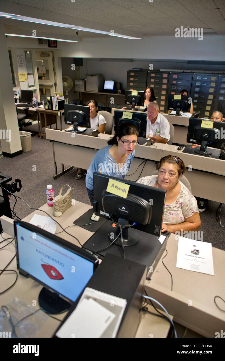 A young Hispanic teacher instructs an older woman at a basic computer ...