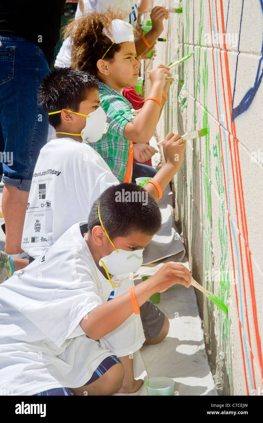 Volunteer artists paint a wall mural as part of a community ...