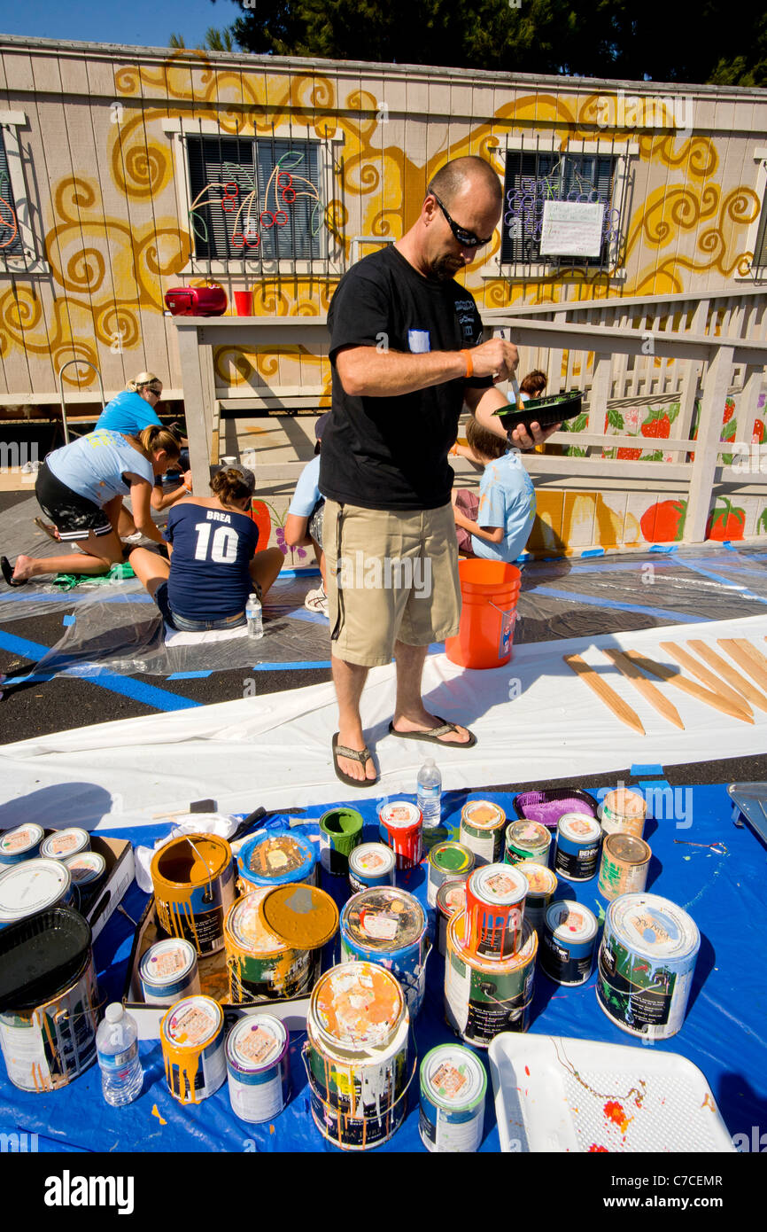 Volunteers in logo T-shirts mix paint at a community beautification ...