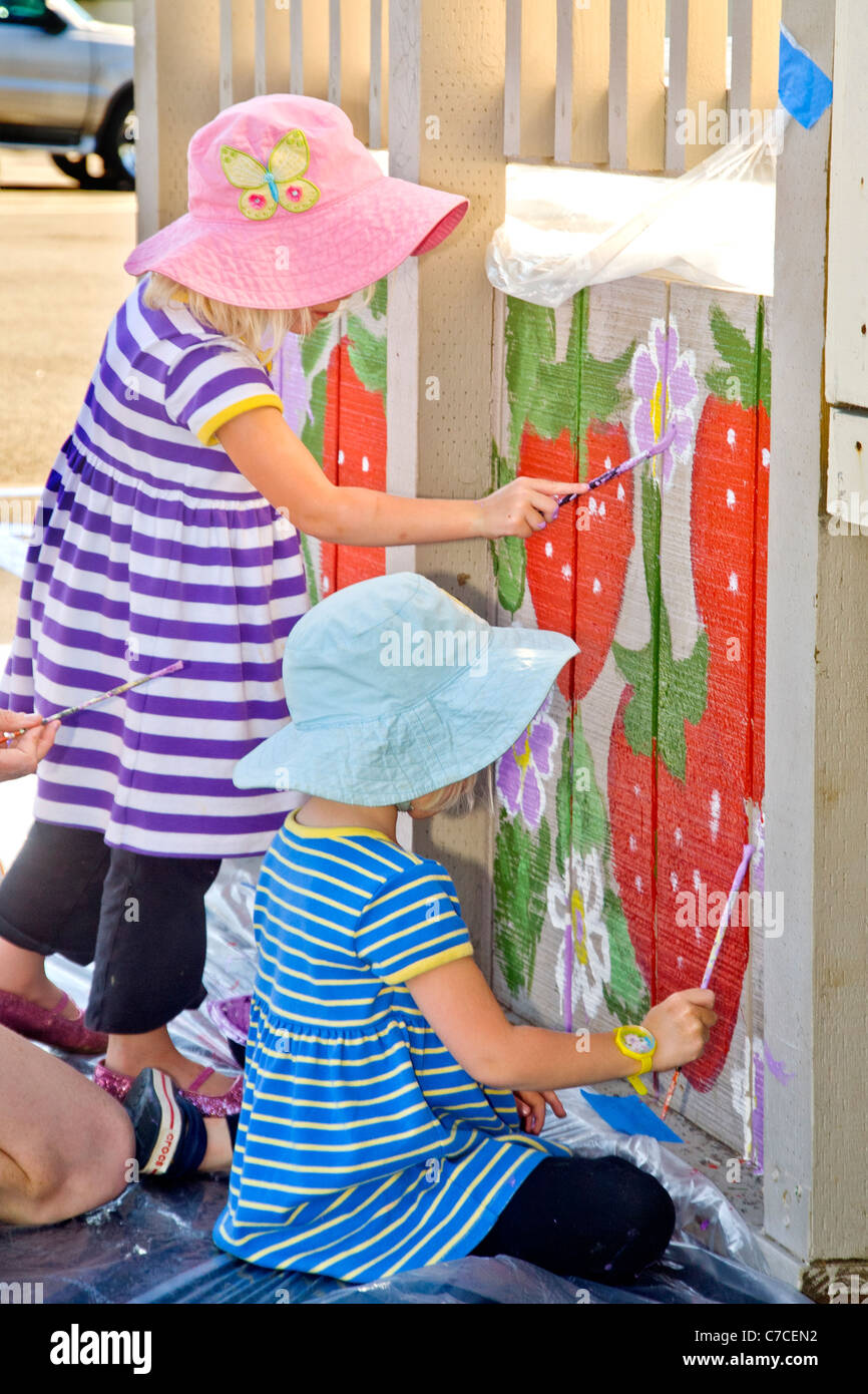 Two young sisters paint decorations on a city building during a ...