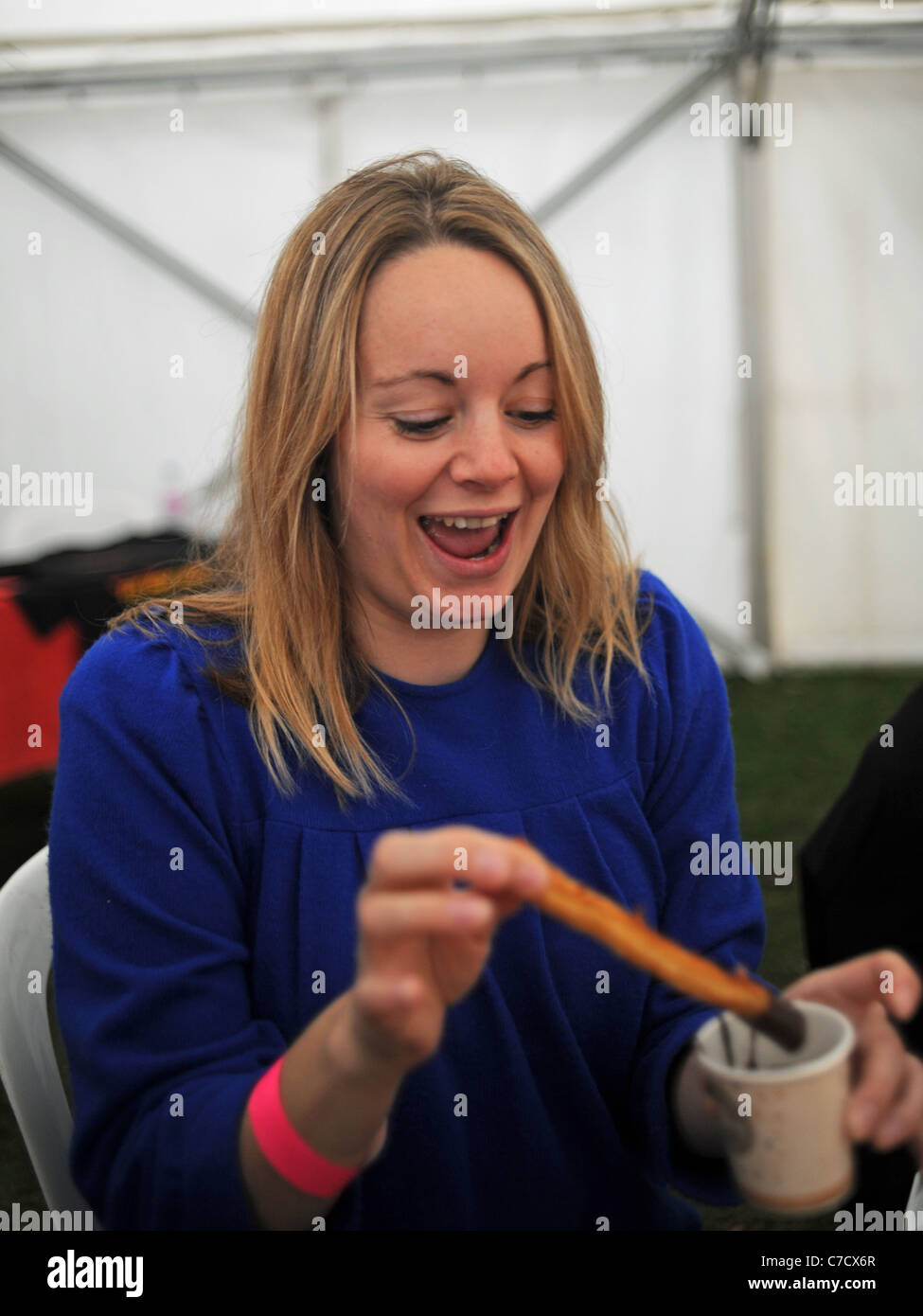 Young woman eating a sugar doughnut stick with chocolate sauce at the ...