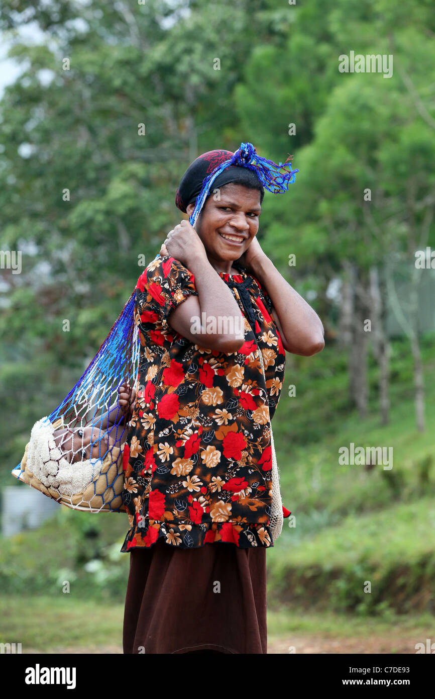 Mother carries her baby boy in a traditional woven bilum hanging from ...