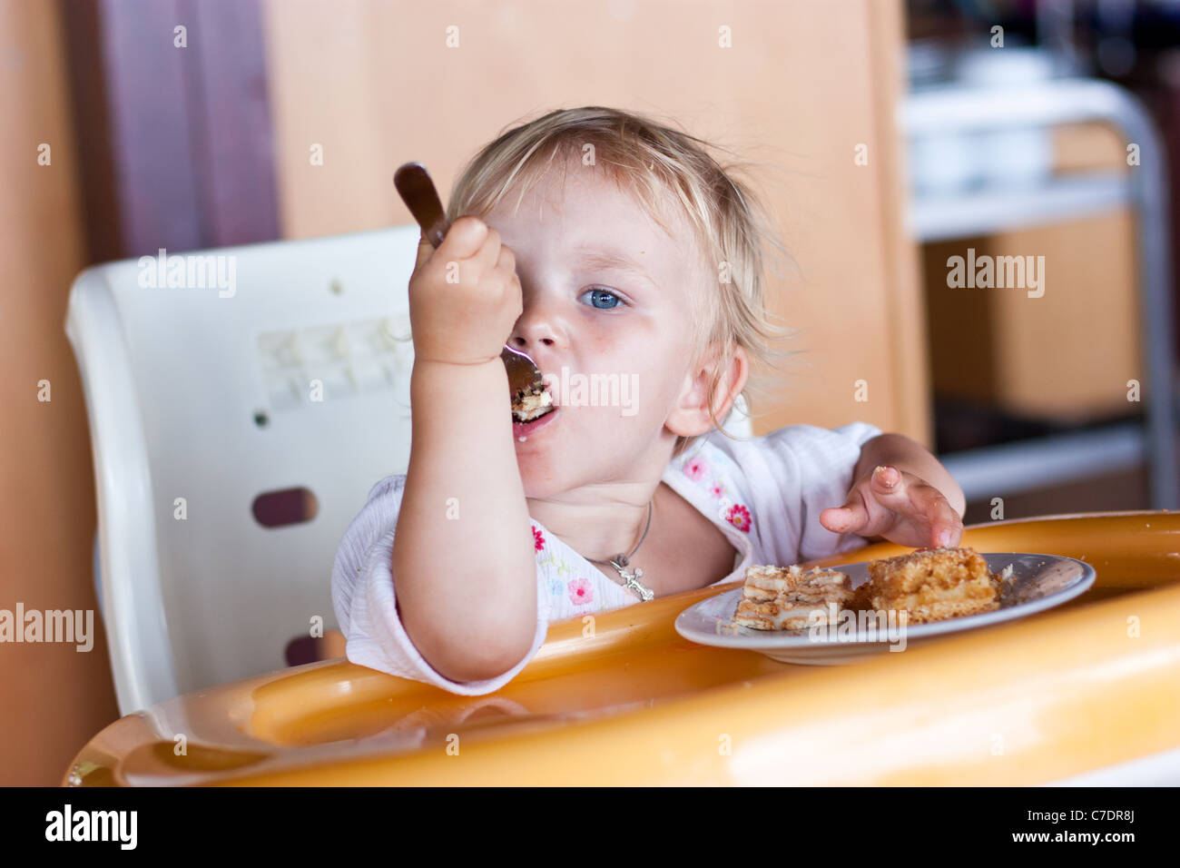 Cute child eating with a fork in a chair Stock Photo - Alamy