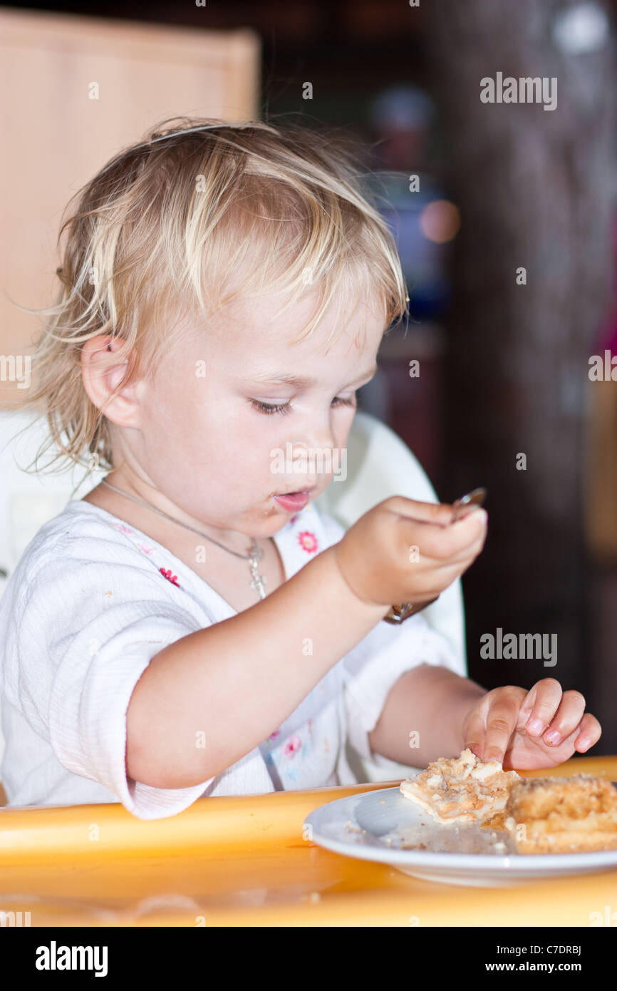 Cute child eating with a fork in a chair Stock Photo - Alamy