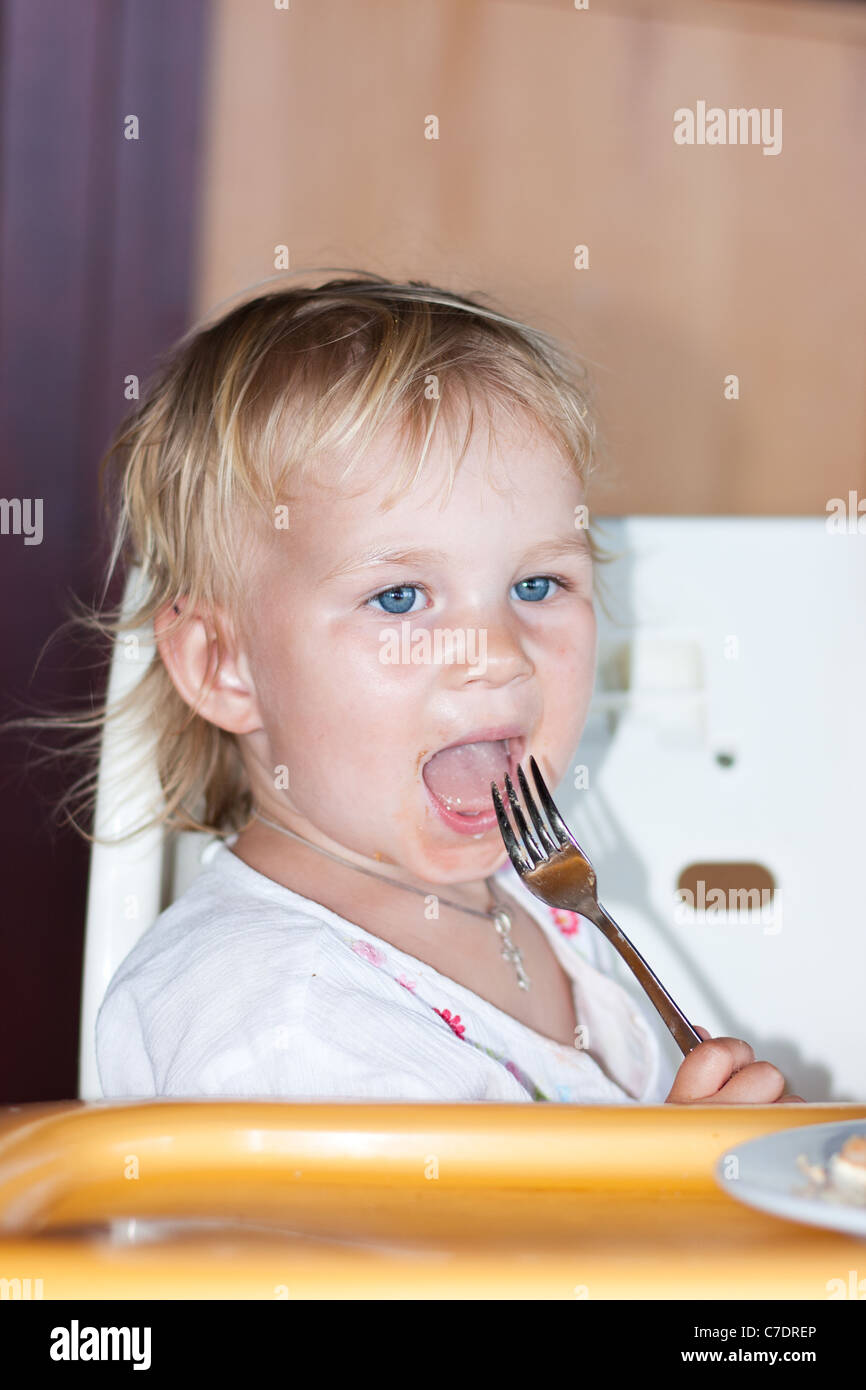 Cute child eating with a fork in a chair Stock Photo - Alamy