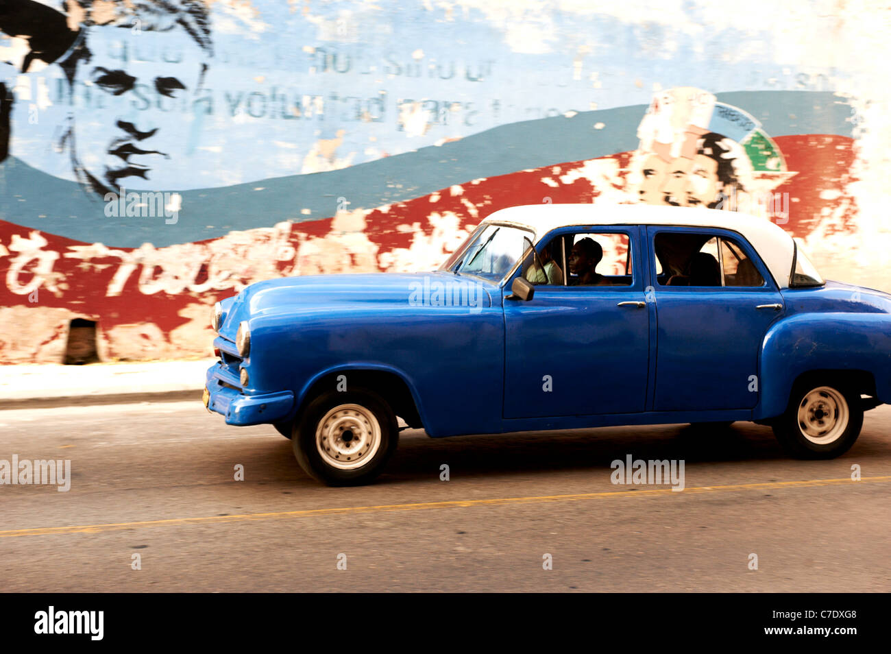 Blue car driving past wall with slogan Havana Cuba Stock Photo - Alamy