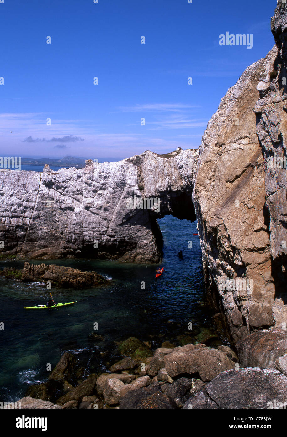 Sea kayakers passing beneath Bwa Gwyn Natural sea rock arch in cliffs ...