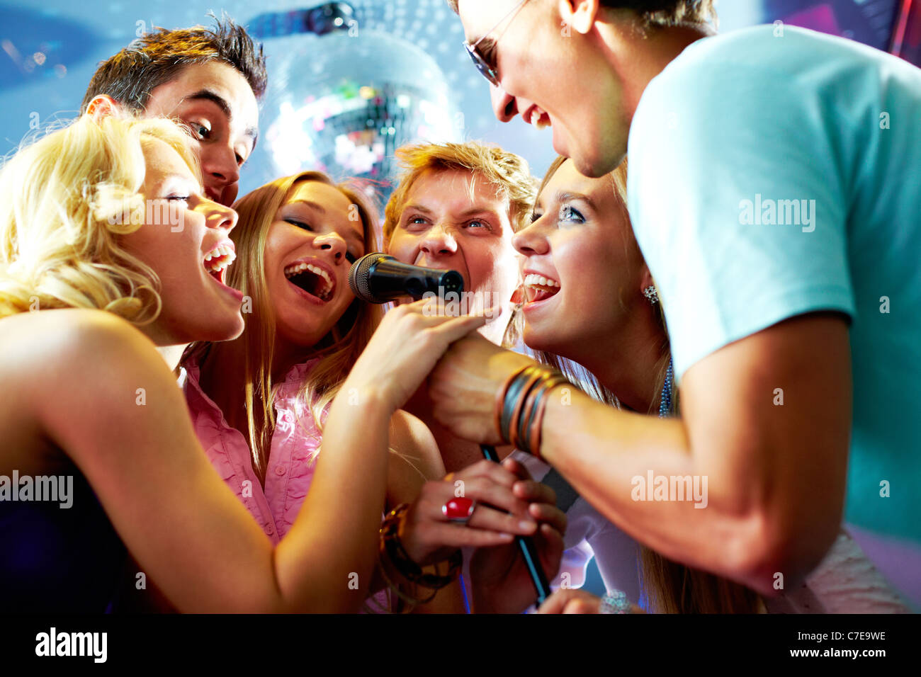 Portrait of joyous guys and girls singing at party in one microphone ...