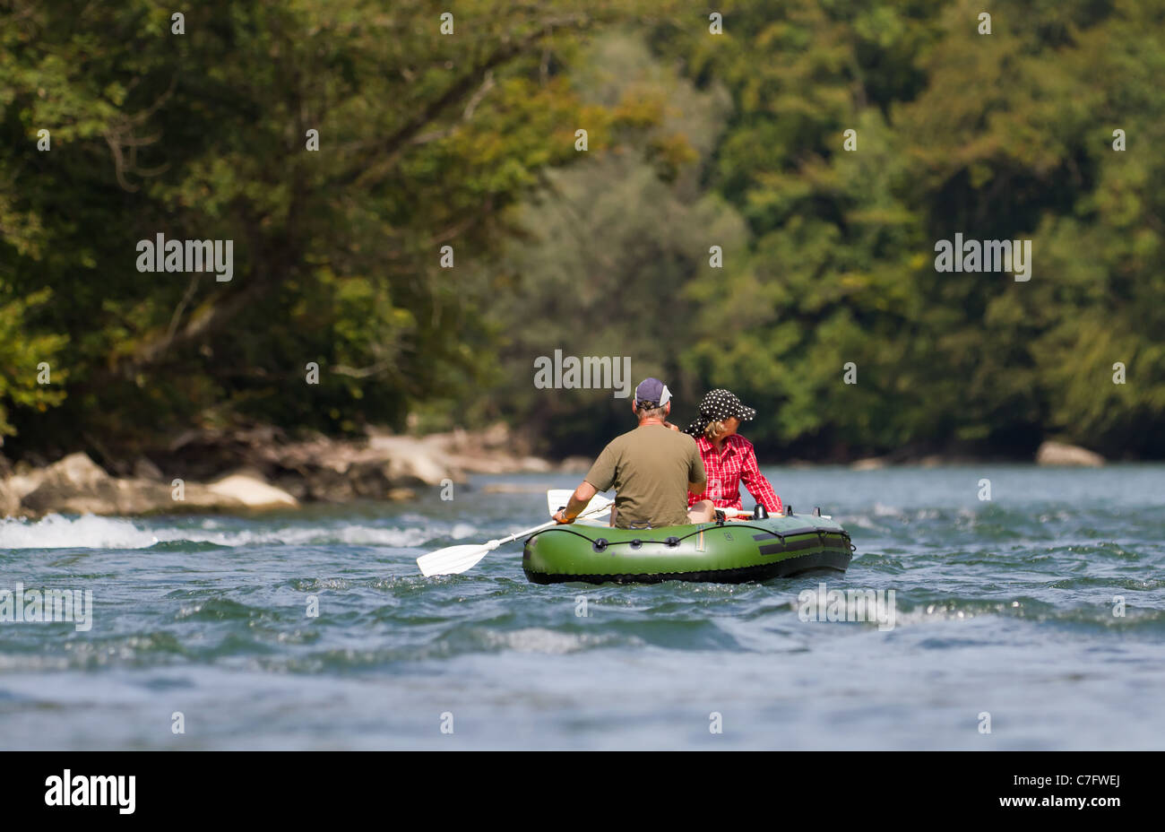 middle aged couple sits in rubber dinghy paddle in hand rowing together ...