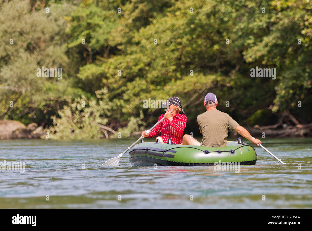middle aged couple sits in rubber dinghy paddle in hand rowing together ...