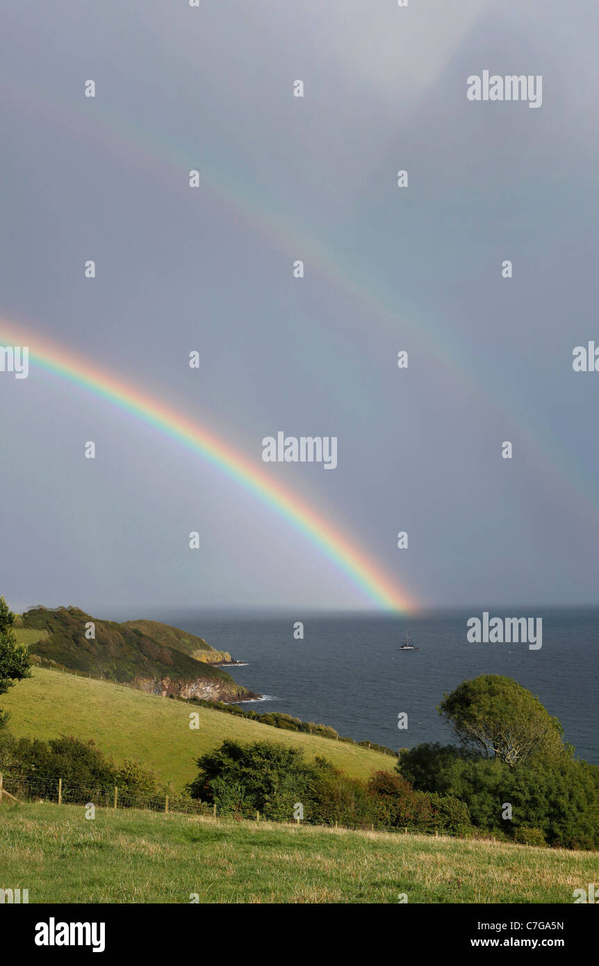 A colorful double rainbow shinning over the sea with dark rain clouds ...