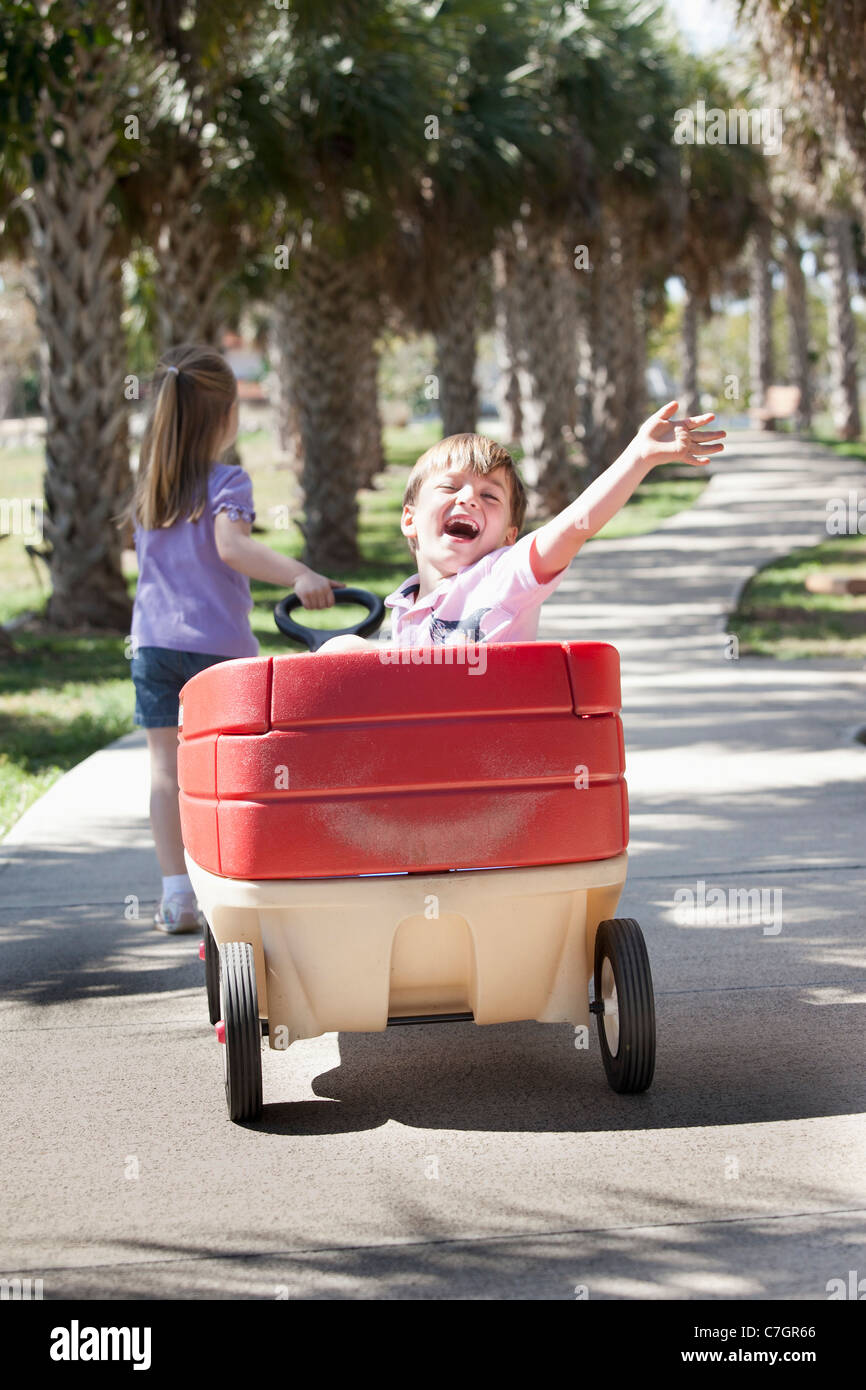 A girl pulling a wagon while a boy is sitting within and waving Stock ...