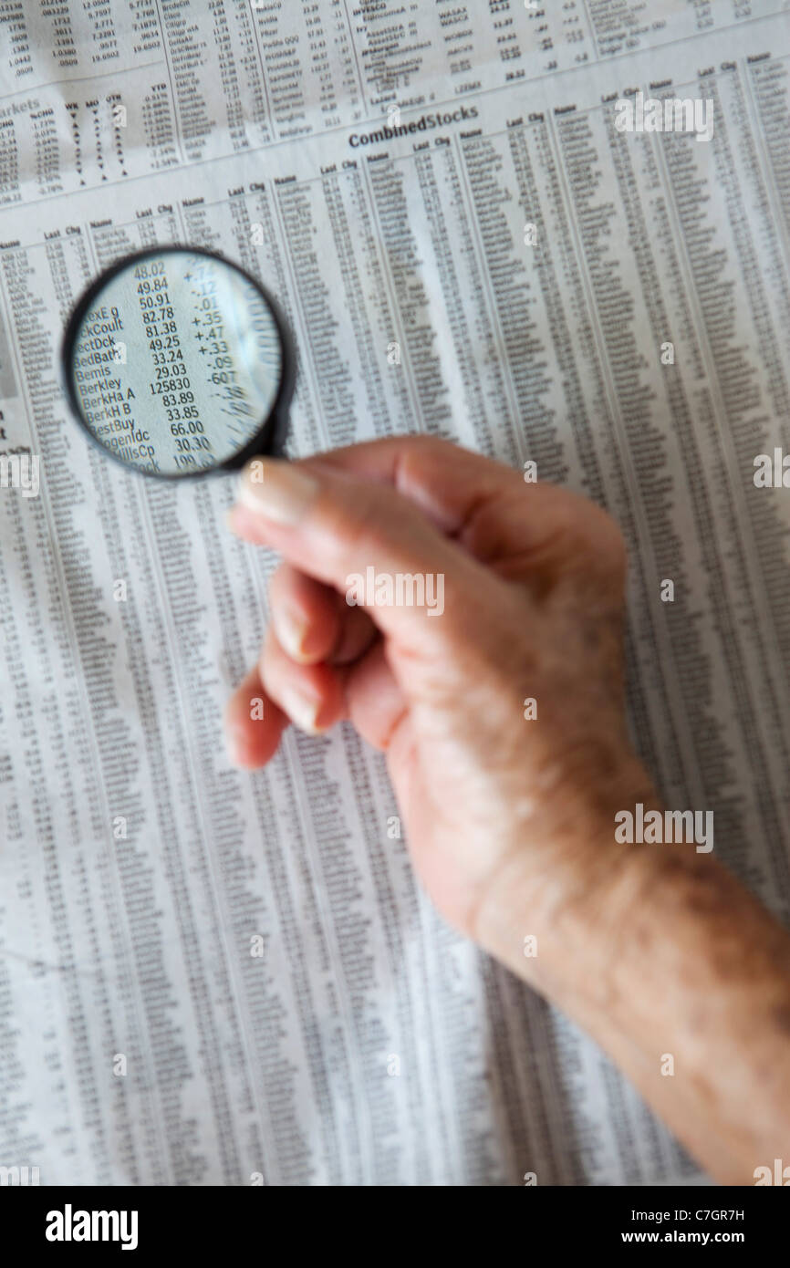 Detail of a senior woman holding a magnifying glass over newspaper ...