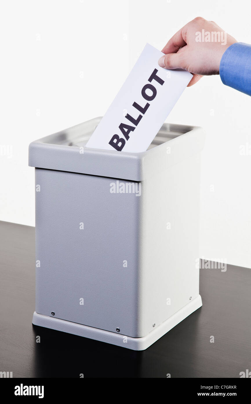 A man putting a paper with the word BALLOT written on it into a ballot ...