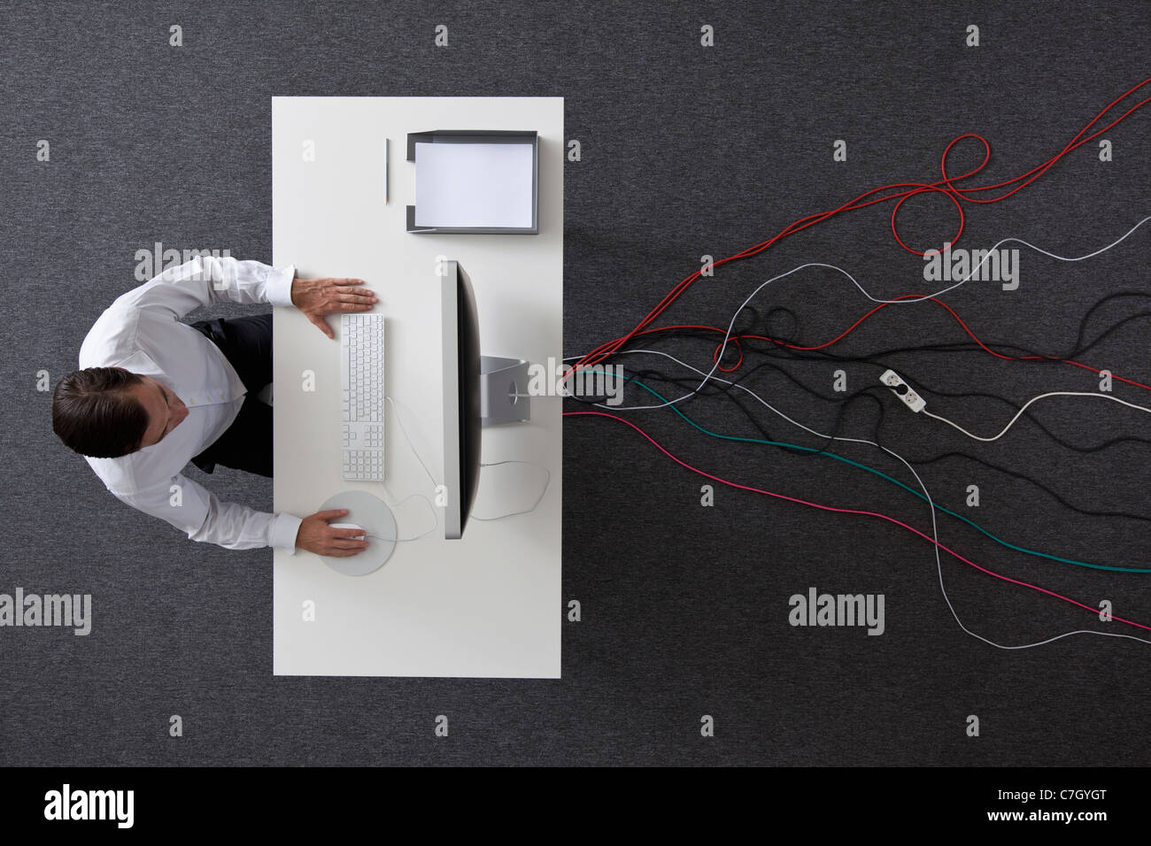 A businessman working at a desk with multiple cables running under it ...