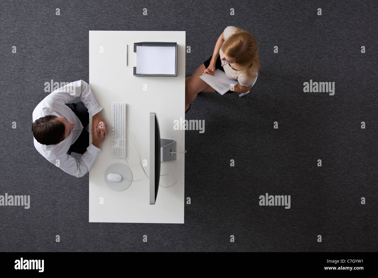 A businessman and businesswoman sitting across a desk from each other ...