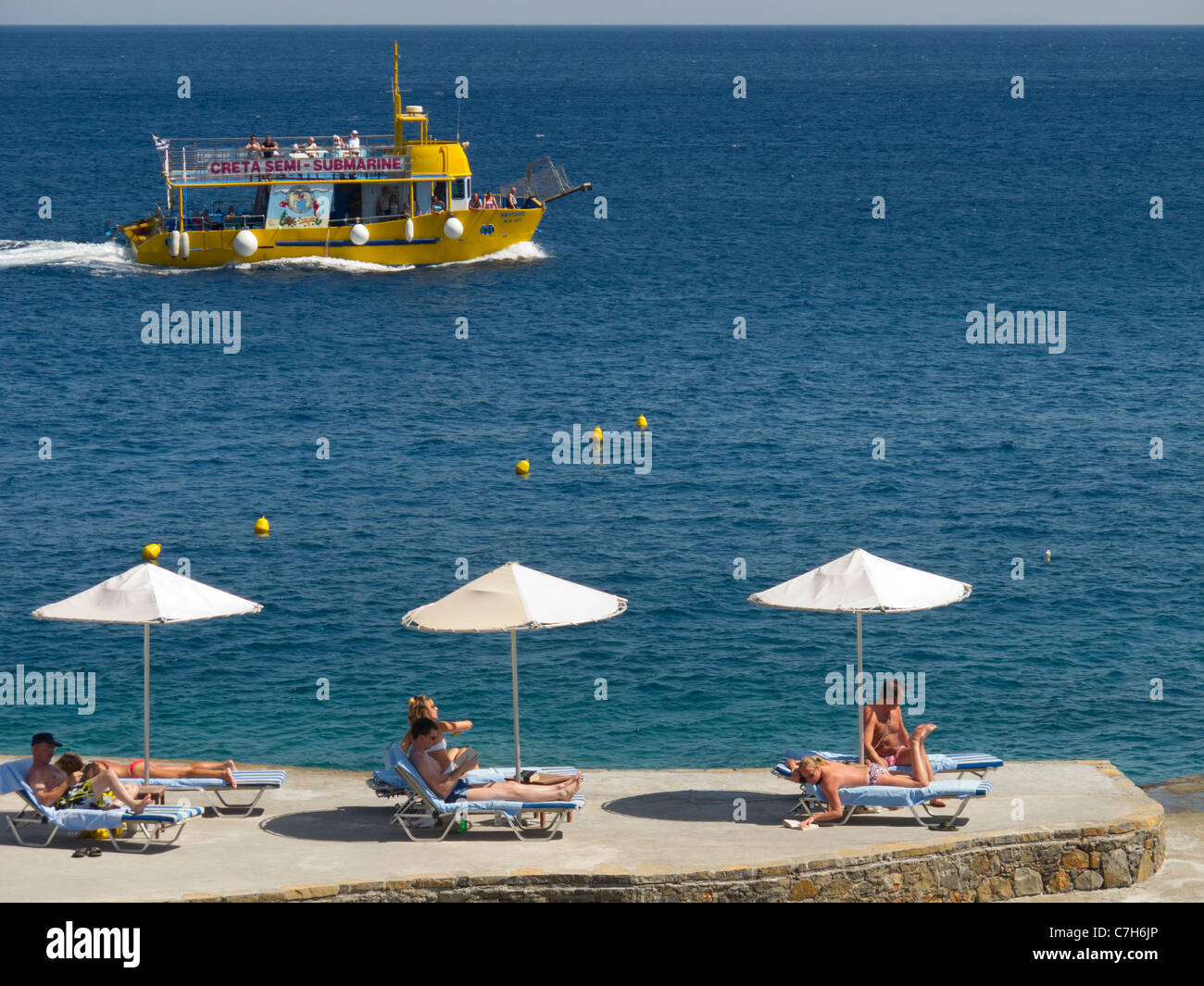 A yellow submarine holiday excursion boat passes tourists sunbathing on ...