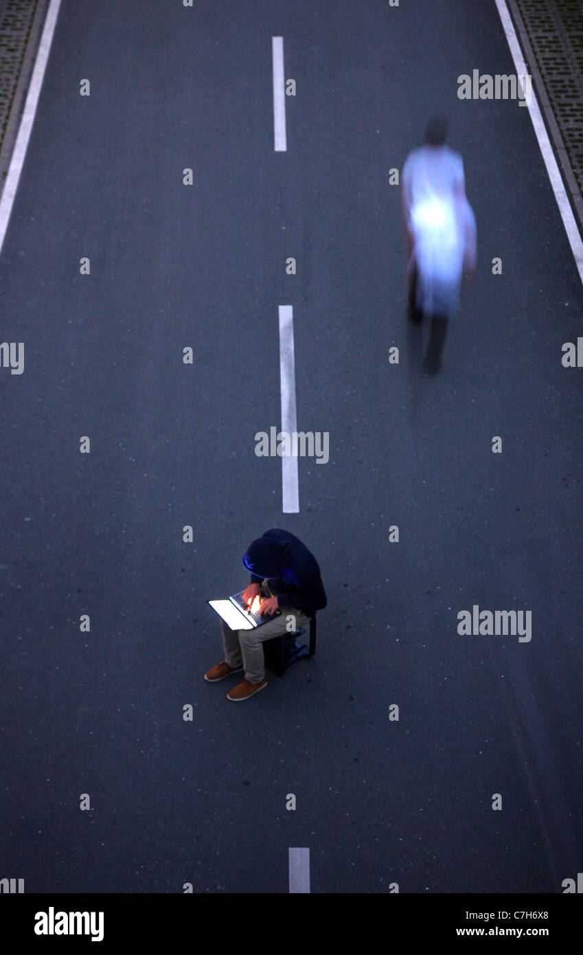 Computer user, hacker, sits conspiratorially, outside, with a laptop ...