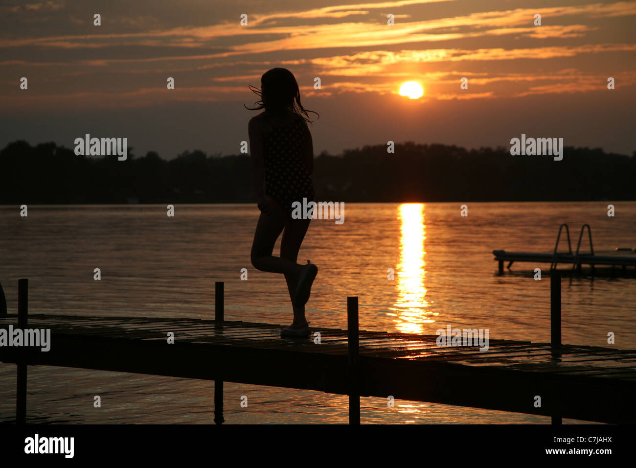 girl running on jetty with sun setting over lake Stock Photo - Alamy