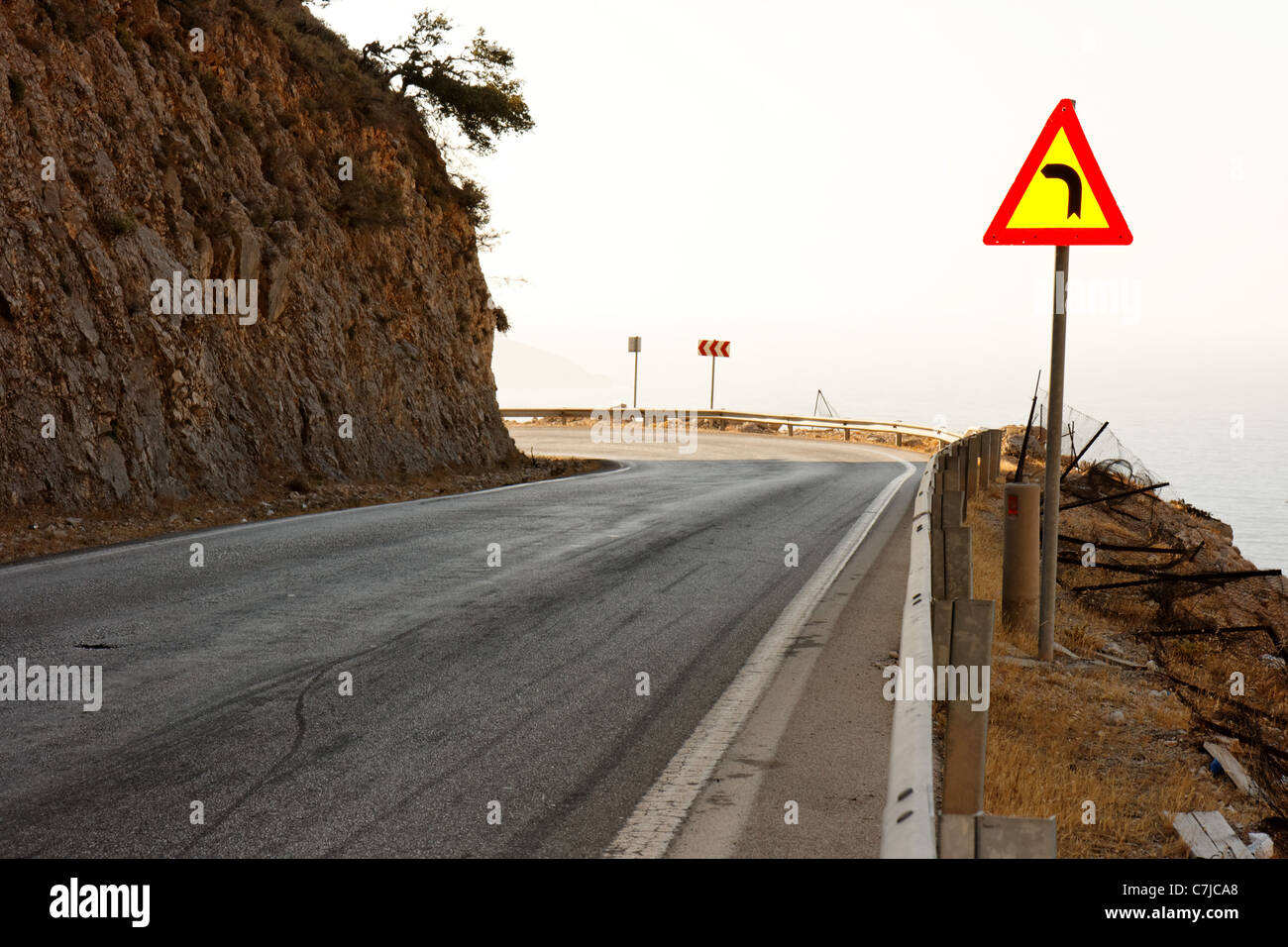 Sign indicates sharp left turn on cliffside road on Kefalonia Stock ...