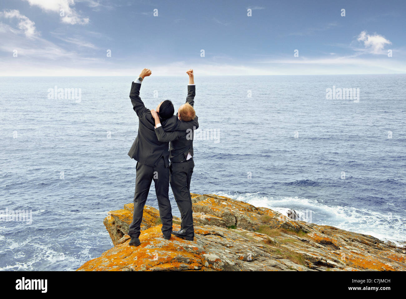 Businessmen cheering on cliff Stock Photo - Alamy
