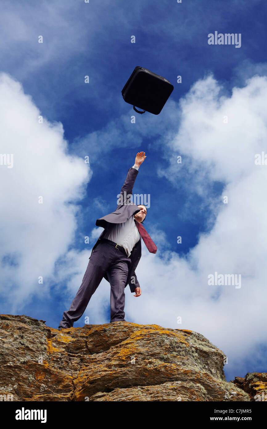 Businessman throwing briefcase off cliff Stock Photo - Alamy