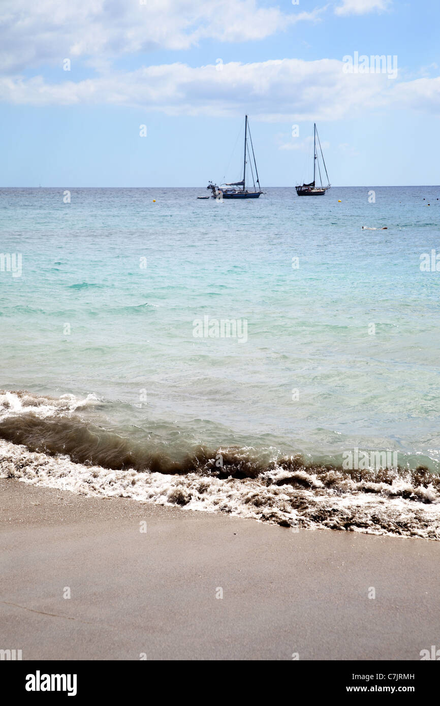 Sandy beach with surf and two sailing yachts Stock Photo - Alamy