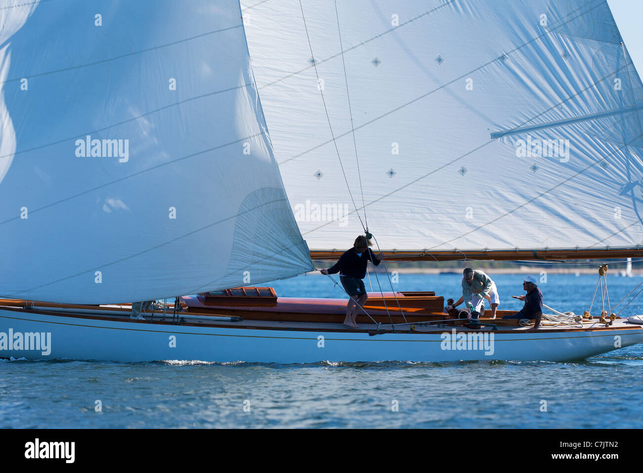 A crew pulls the tack of the headsail in after completing a tack on ...