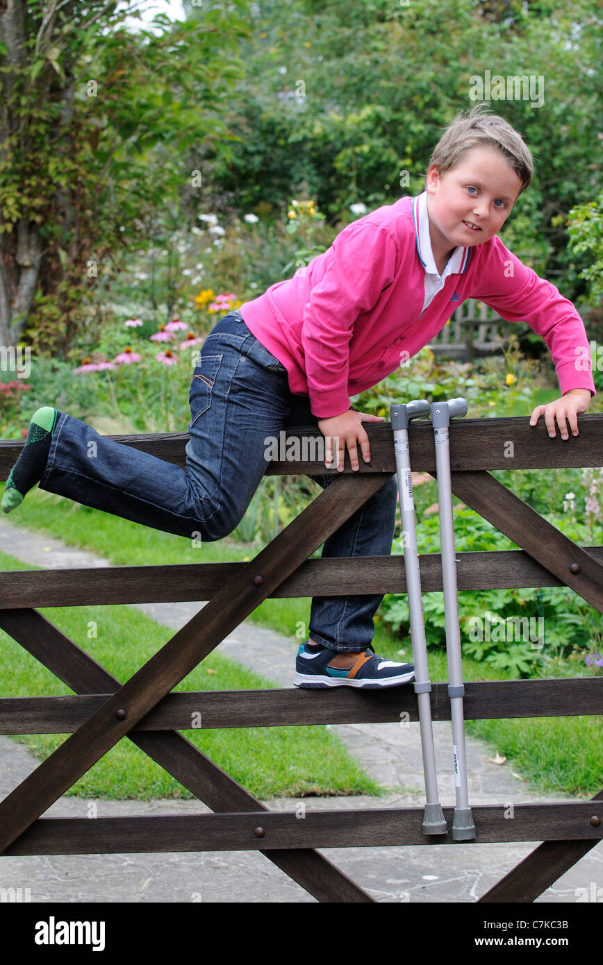 Young boy with injured foot and walking sticks climbing over a garden ...