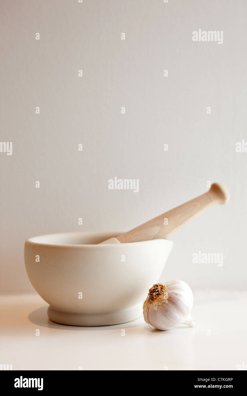 A mortar and pestle with a clove of garlic against a white background ...